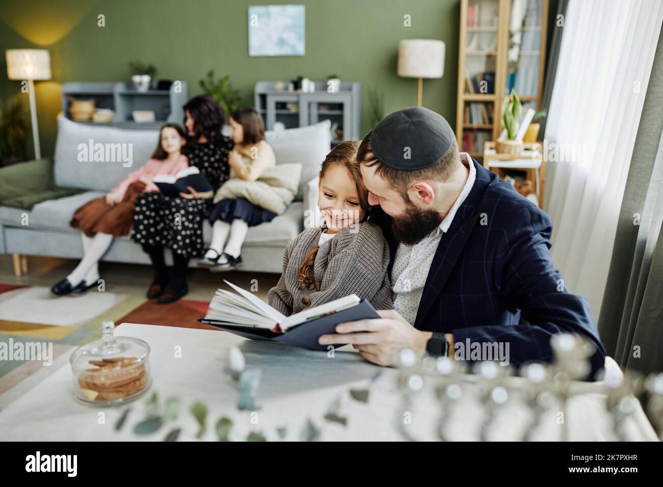 Portrait of smiling jewish father reading book to daughter while ...