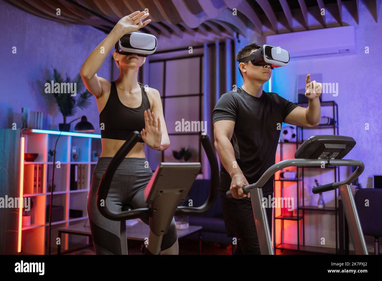 Joyful caucasian woman training on exercise bike with sporty asian man ...