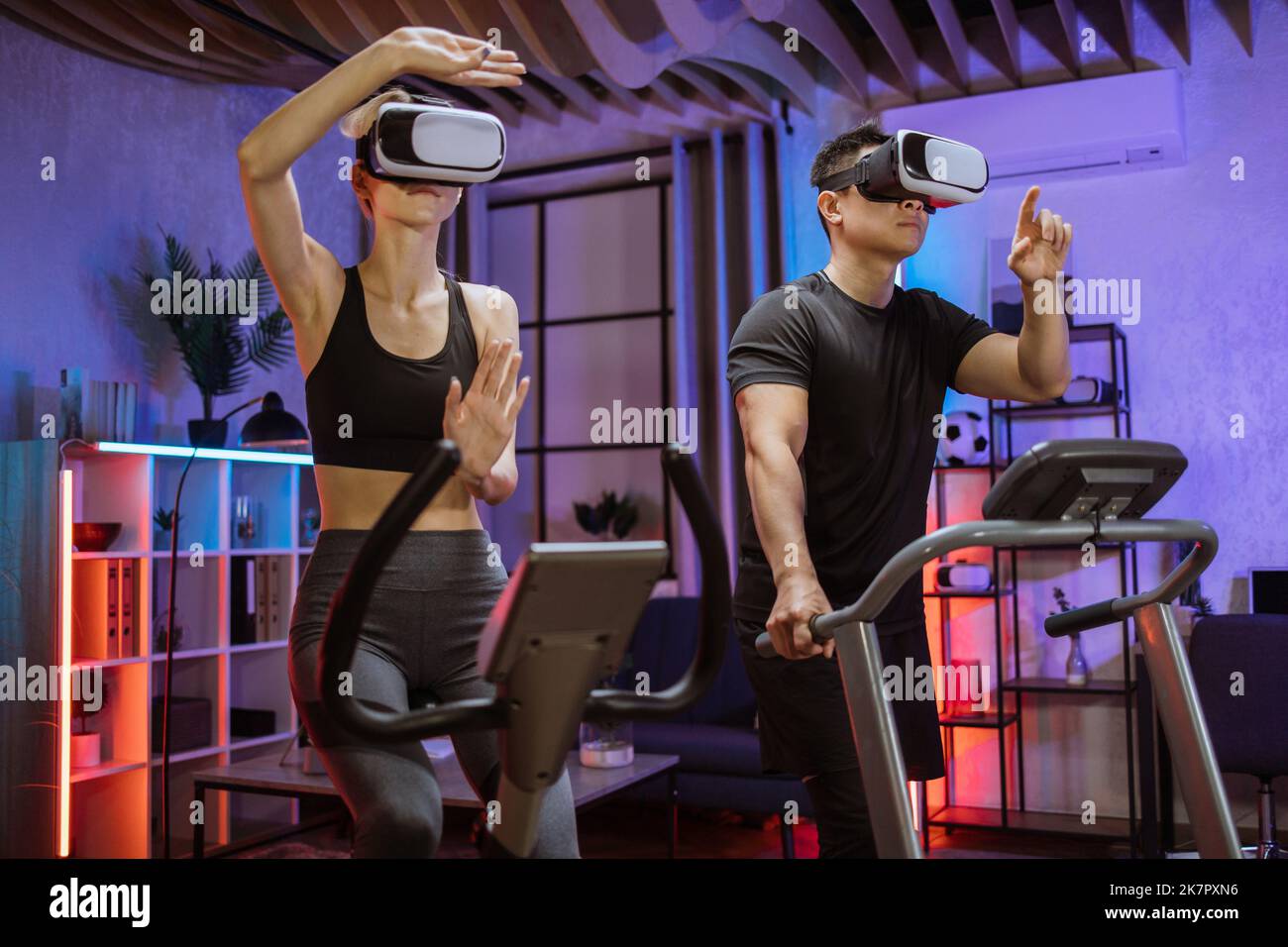 Joyful caucasian woman training on exercise bike with sporty asian man ...