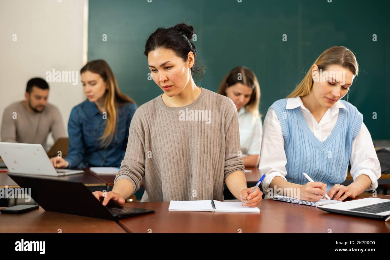 Students writing in notebook and typing on laptop during class in ...