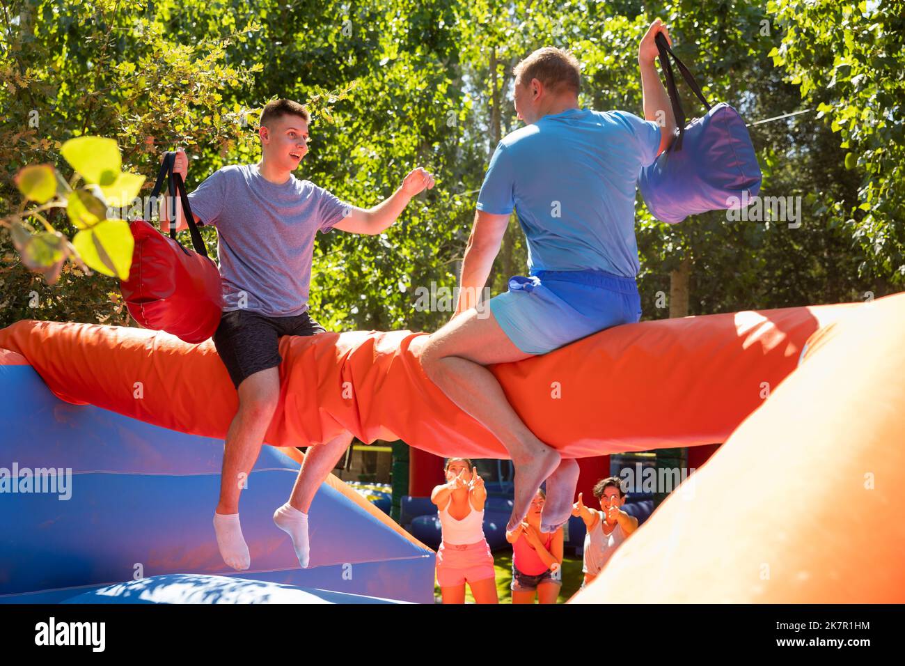 Cheerful teenager having fun with father on inflatable pillow fight ...