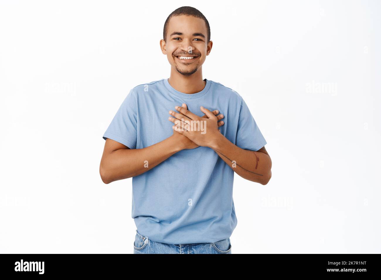 Smiling nice guy holds hands on heart, heartwarming and caring feeling ...