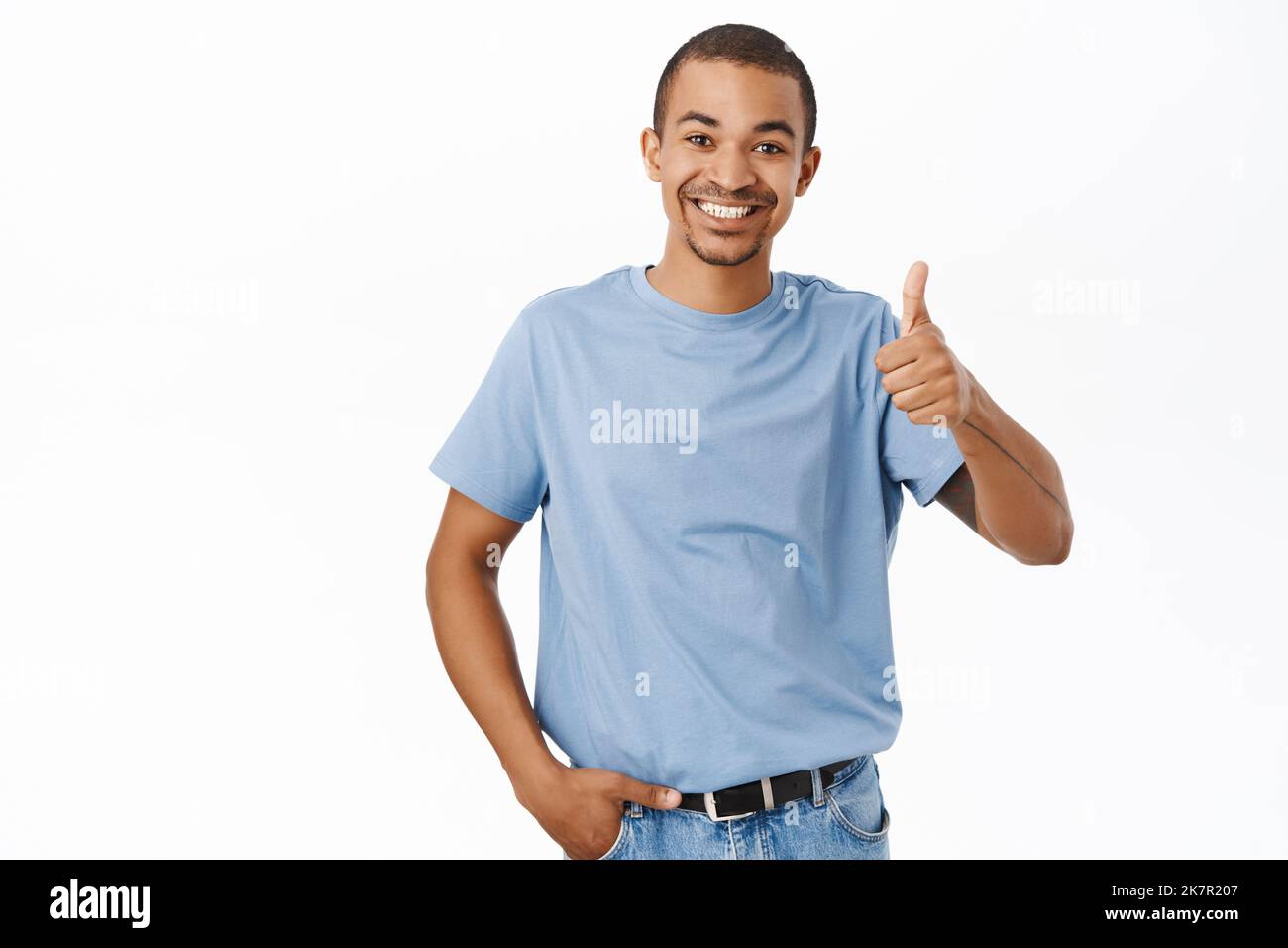 Cheerful young man shows thumbs up and smiling, approve, supports smth ...