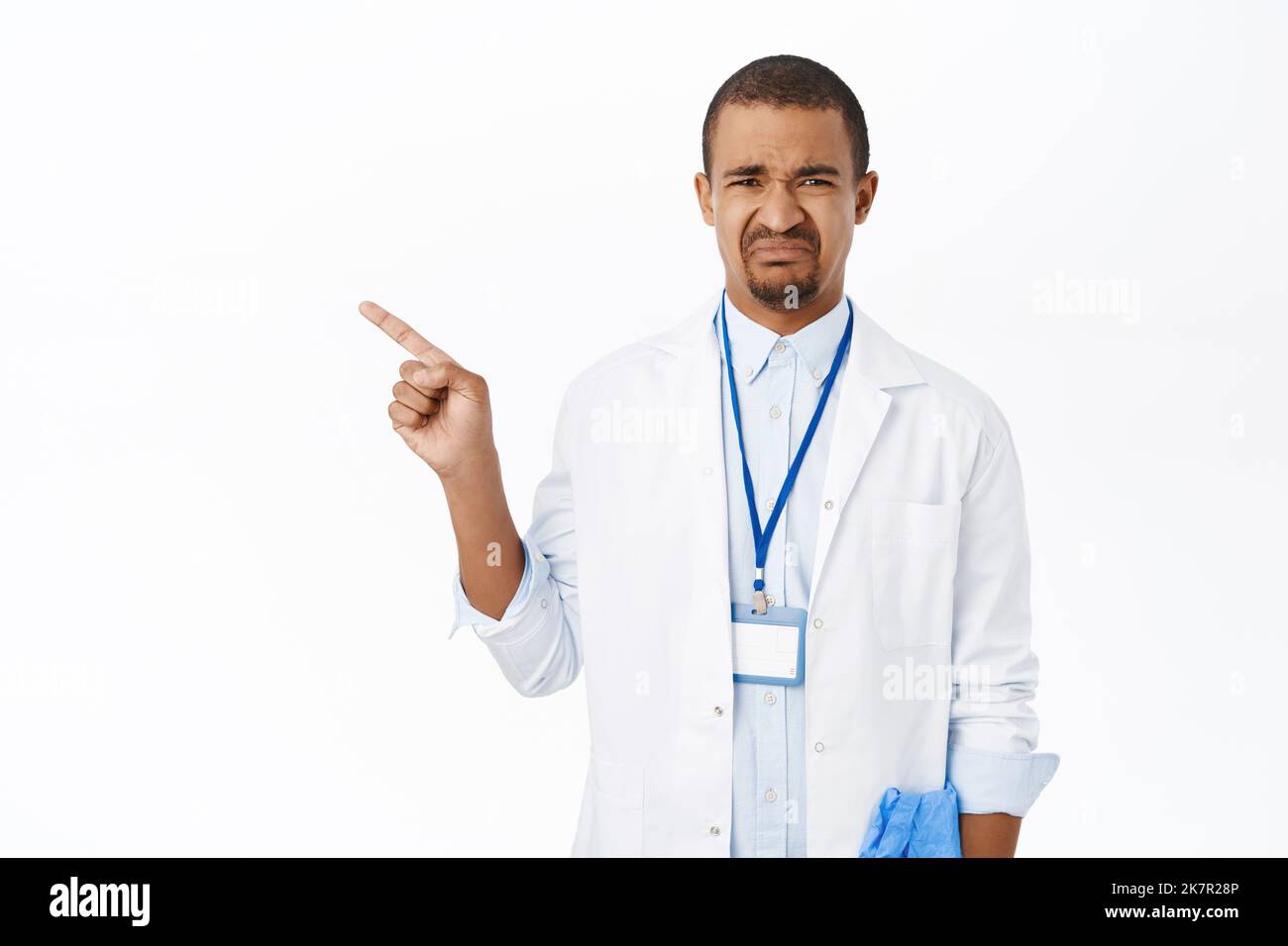 Sad male physician, doctor pointing left, grimacing and looking ...