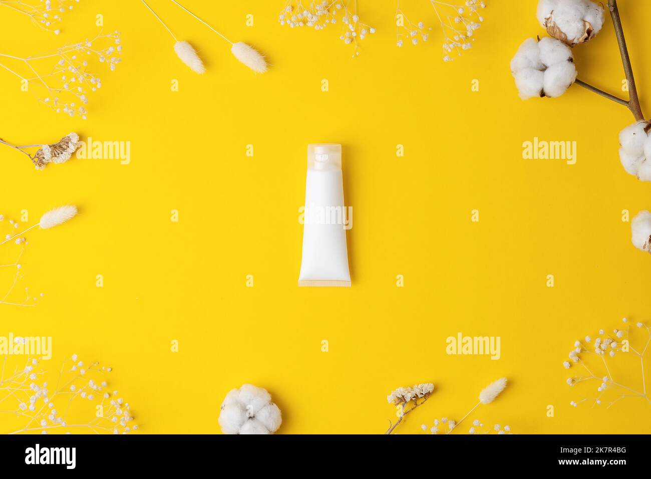 White tube of cosmetic cream with flowers on yellow background. Flat ...