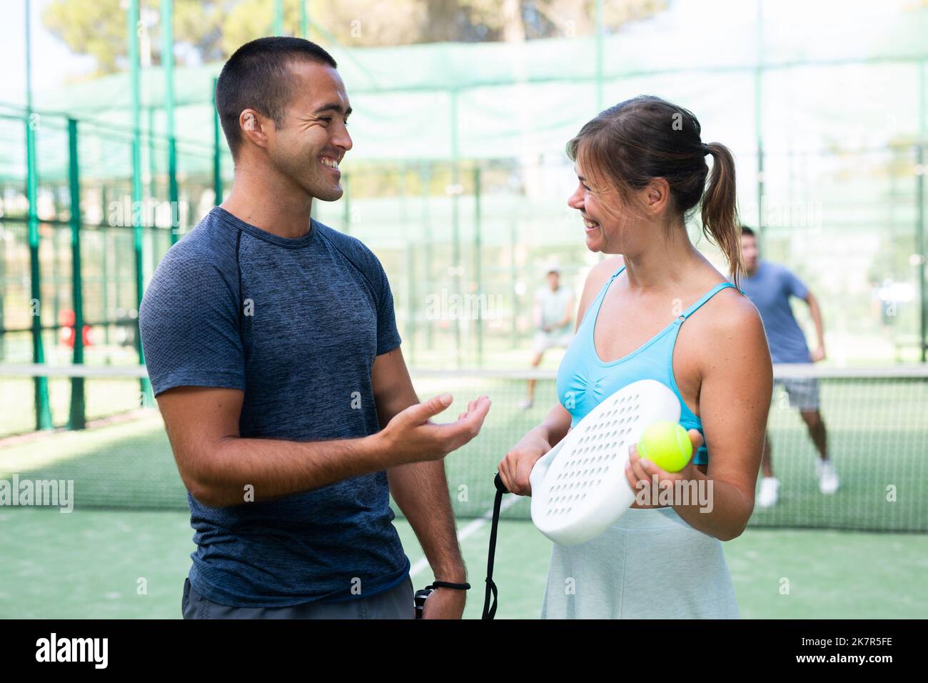 Cheerful man and woman paddle tennis players talking on open court ...