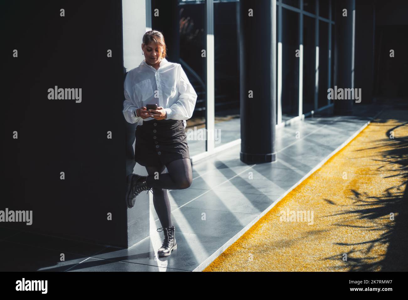 A plus-size Hispanic businesswoman leaning against the black wall of an ...