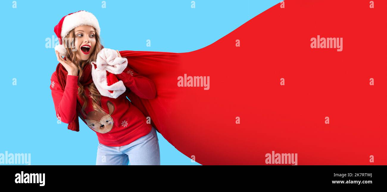 Surprised young woman in Santa hat and with big bag on light blue ...