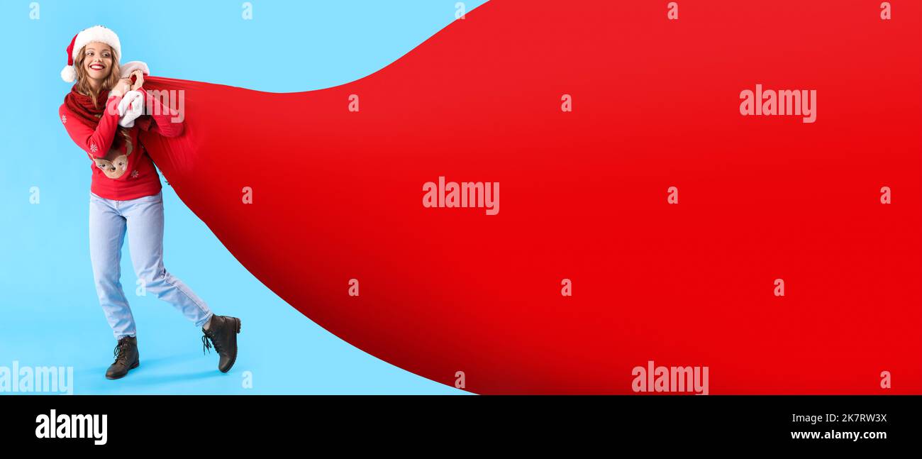 Beautiful young woman in Santa hat and with big bag on light blue ...