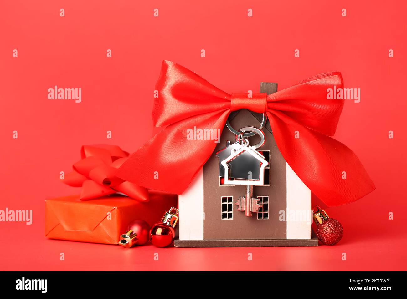 House model with key, bow, Christmas balls and gift on red background ...