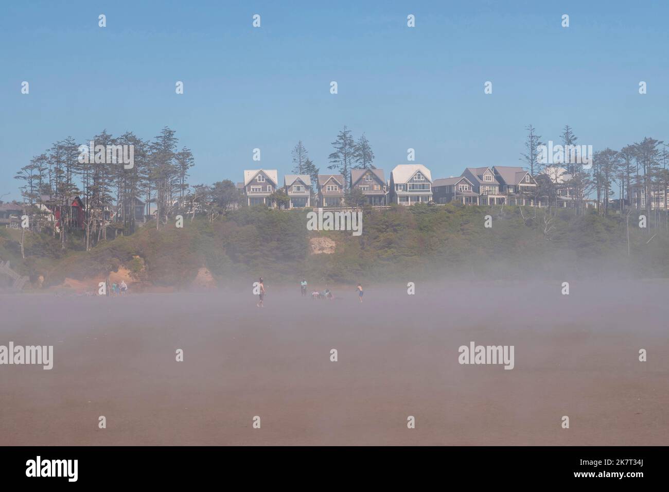 People play on the beach in a heavy mist, with a row of large houses on ...
