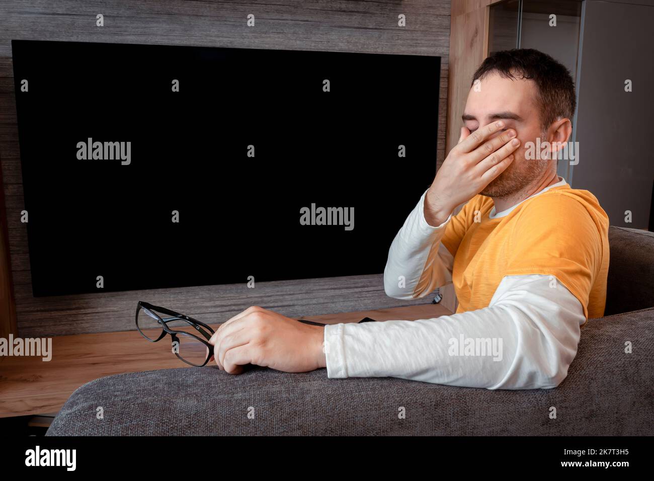 man feeling tired, touching eyes when watching tv at home. fatigue of ...