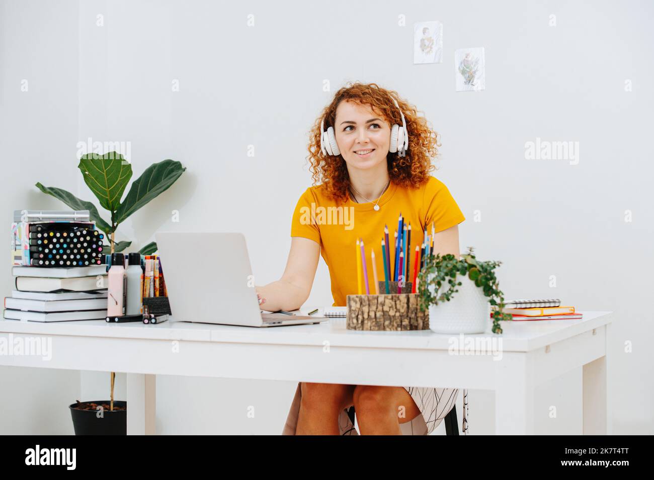 Dreamy young woman with curly ginger hair sitting behind her work desk ...