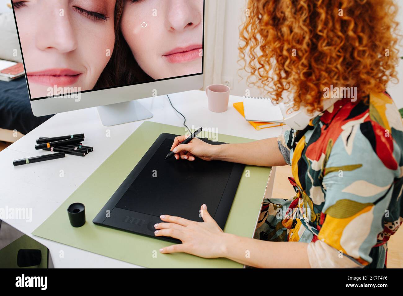 Behind image of a woman working on a graphic tablet, looking at the big ...