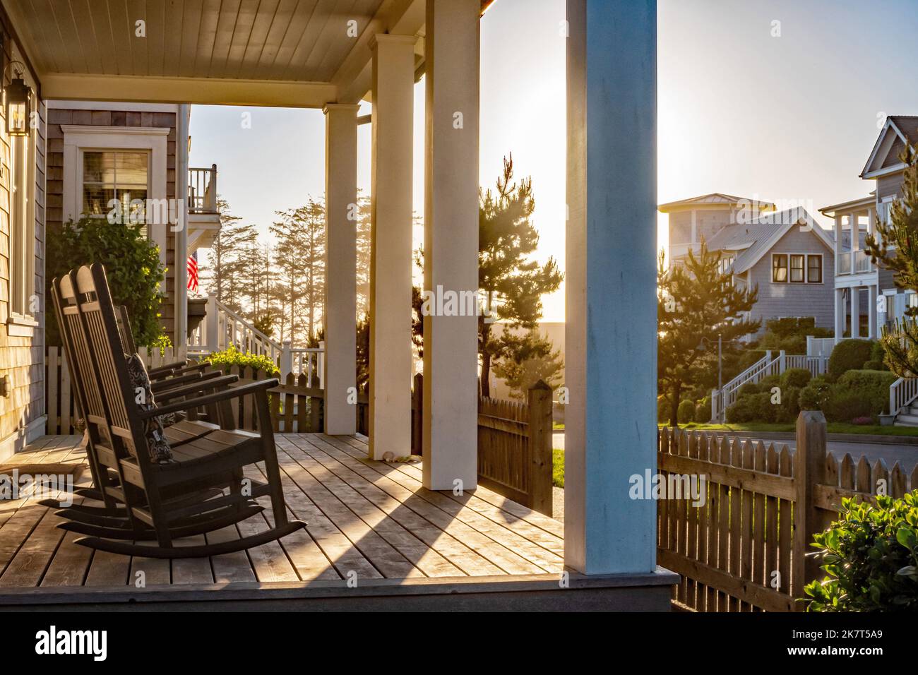 Rocking chairs on a front porch face the glow of evening light off the ...