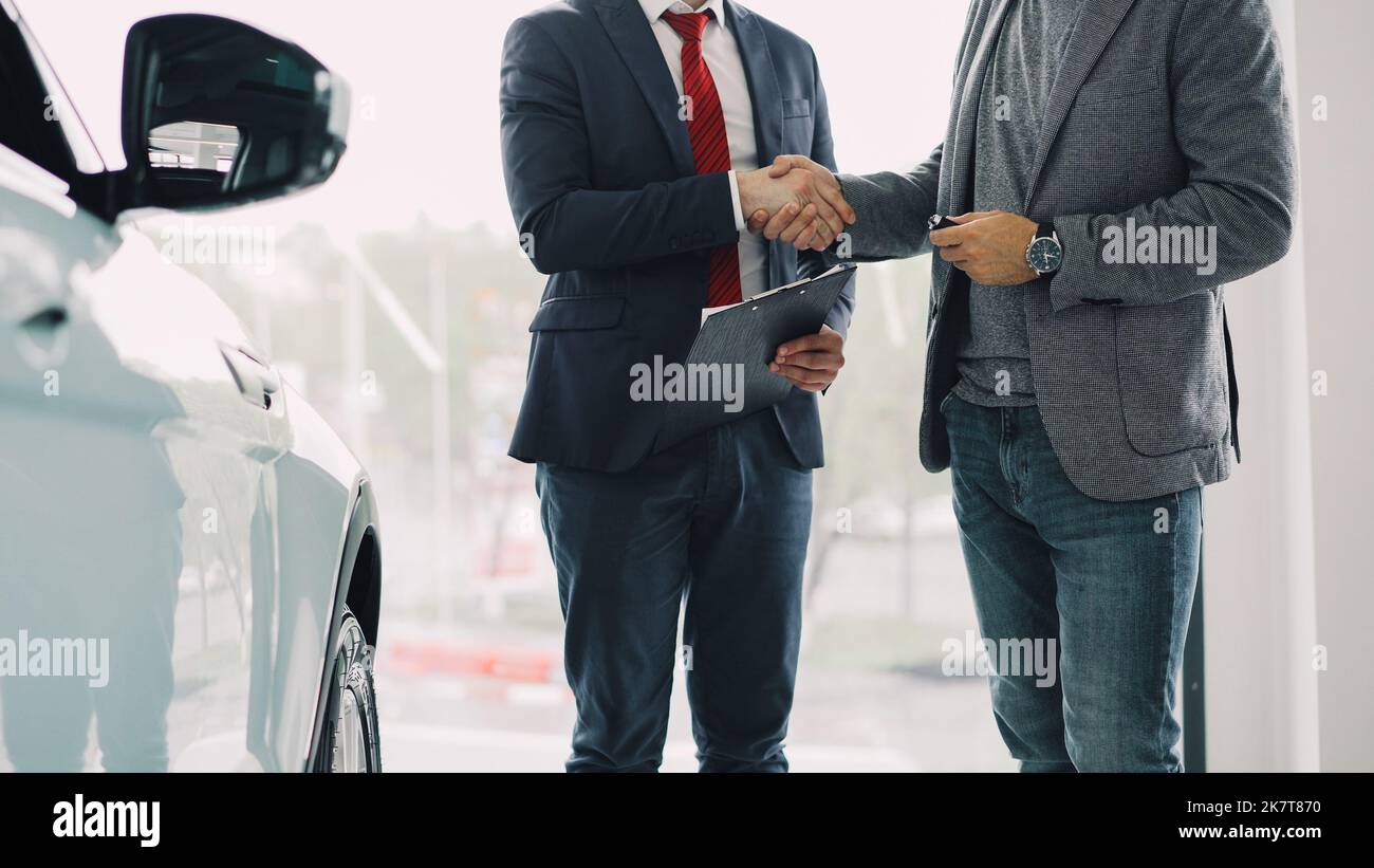 Motor showroom employee is giving car key to young male buyer and ...