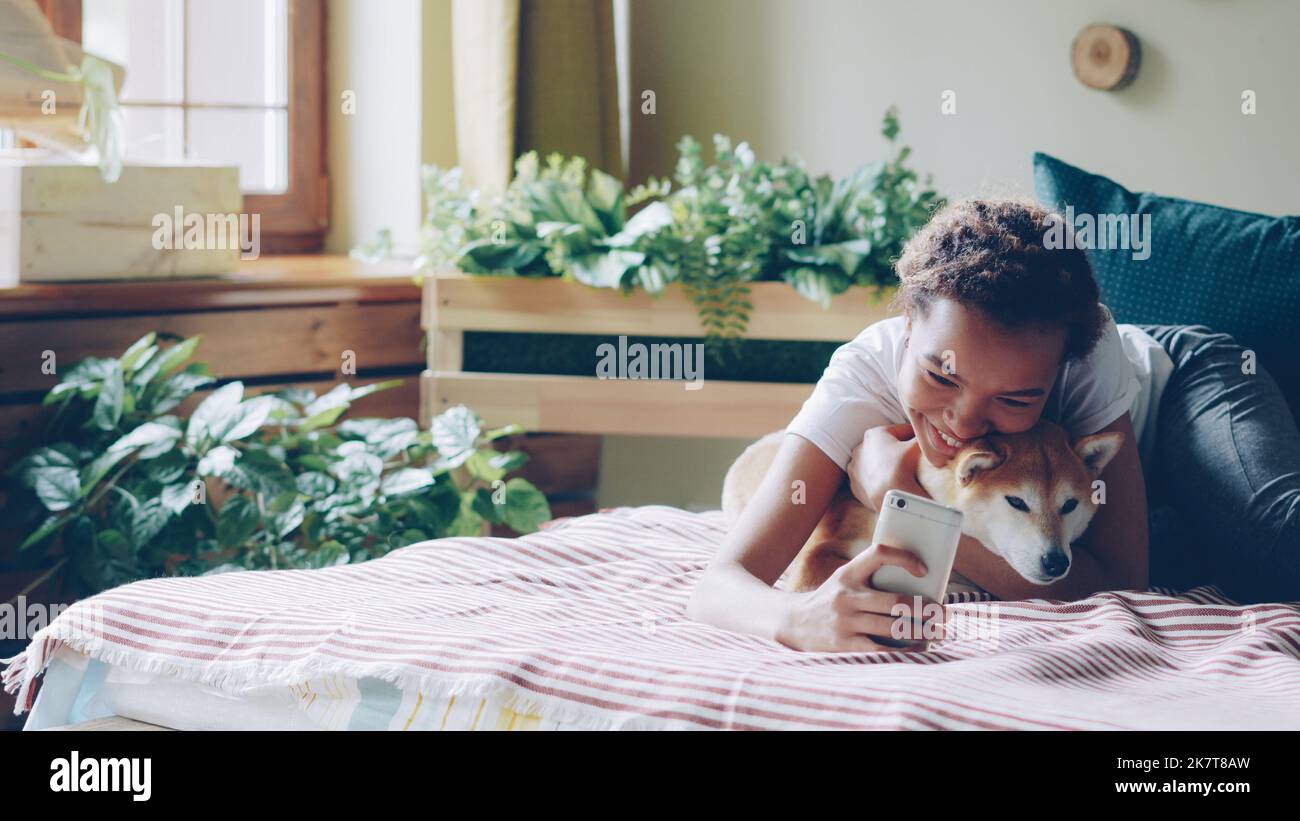 Joyful dog owner is taking selfie with cute friendly pet lying on bed ...
