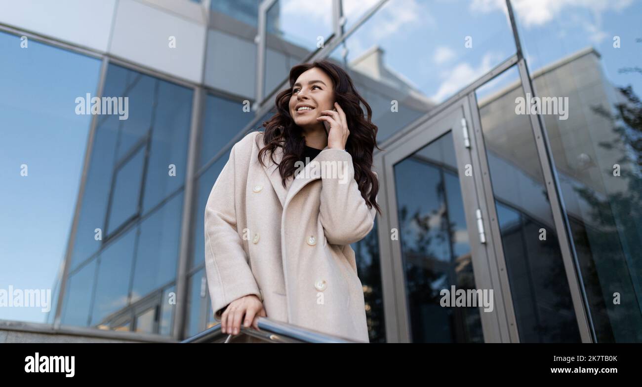 successful confident businesswoman speaks on a mobile phone against the backdrop of an office ...