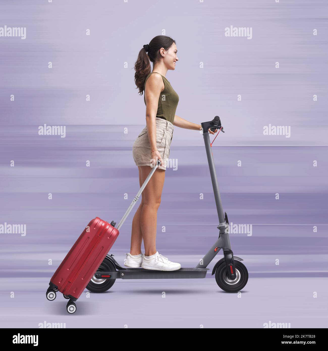 Tourist woman riding a fast electric scooter and carrying a trolley bag ...