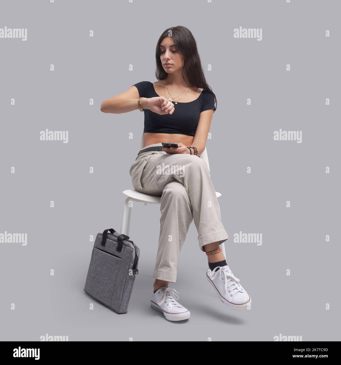 Bored young woman sitting on a chair and waiting, she is checking the ...