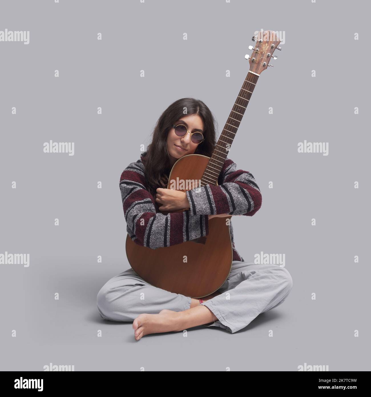 Stylish hippie woman sitting with legs crossed and holding an acoustic ...