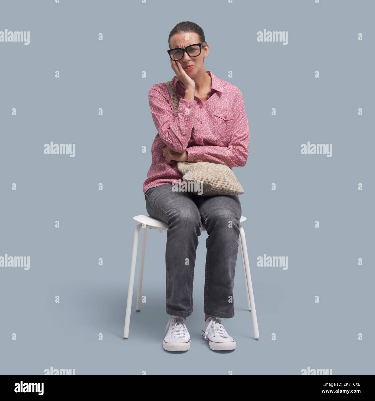 Woman sitting on a chair and touching her cheek, she is having a bad ...