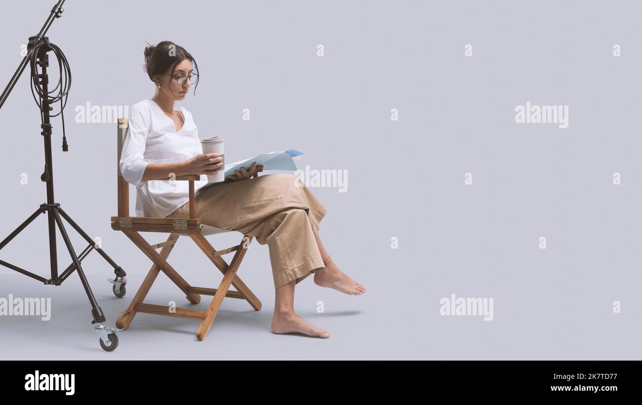 Focused actress sitting on the director's chair and reading a play ...
