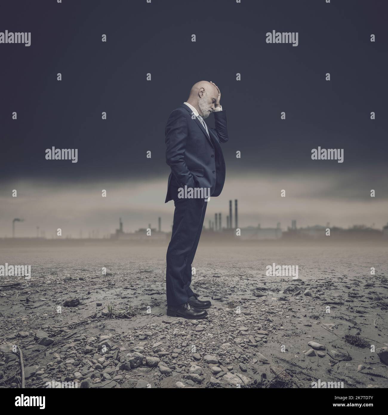 Desperate corporate businessman stading in a dry barren land, polluting ...