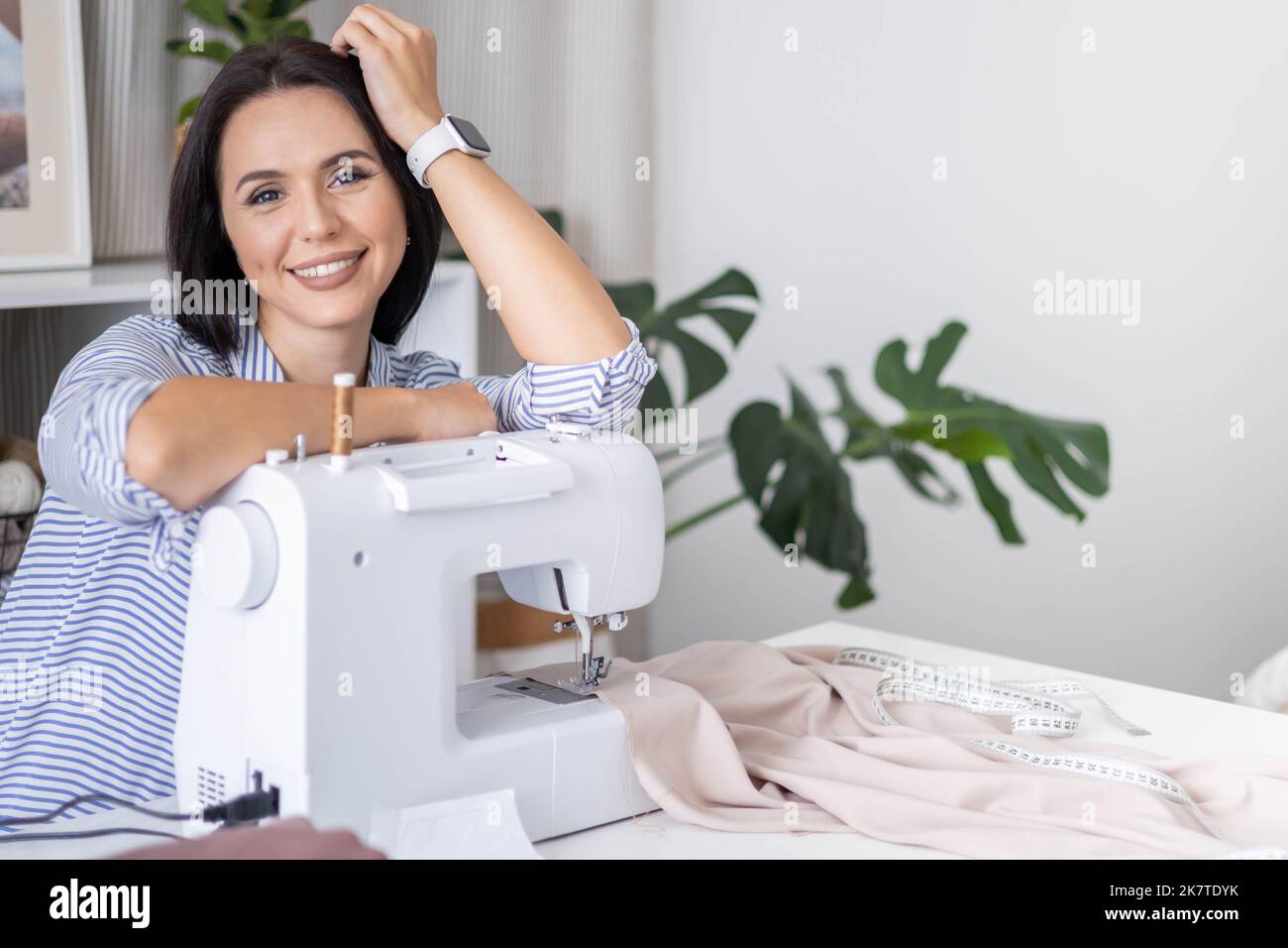 Portrait happy woman tailor dressmaker posing at workplace electric ...