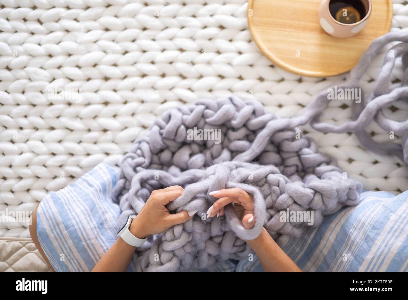 Female hands knitting warm plaid merino wool ribbon yarn sitting on bed ...