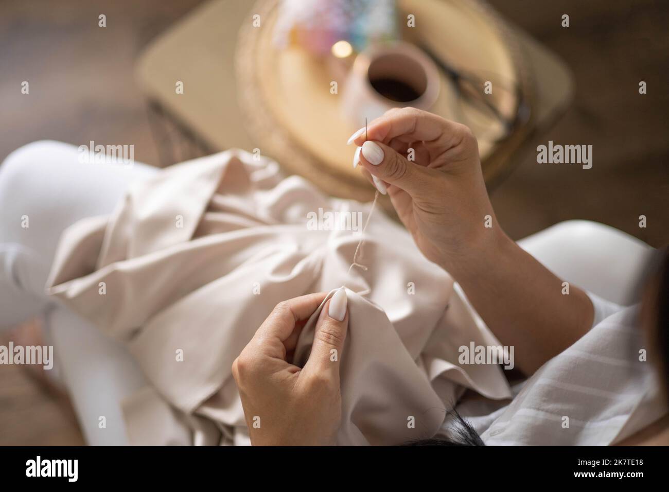 Female tailor hands sewing beige textile with needle and thread process ...