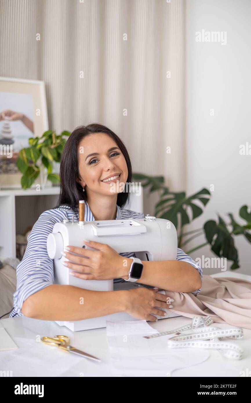 Portrait happy woman tailor dressmaker posing at workplace electric ...
