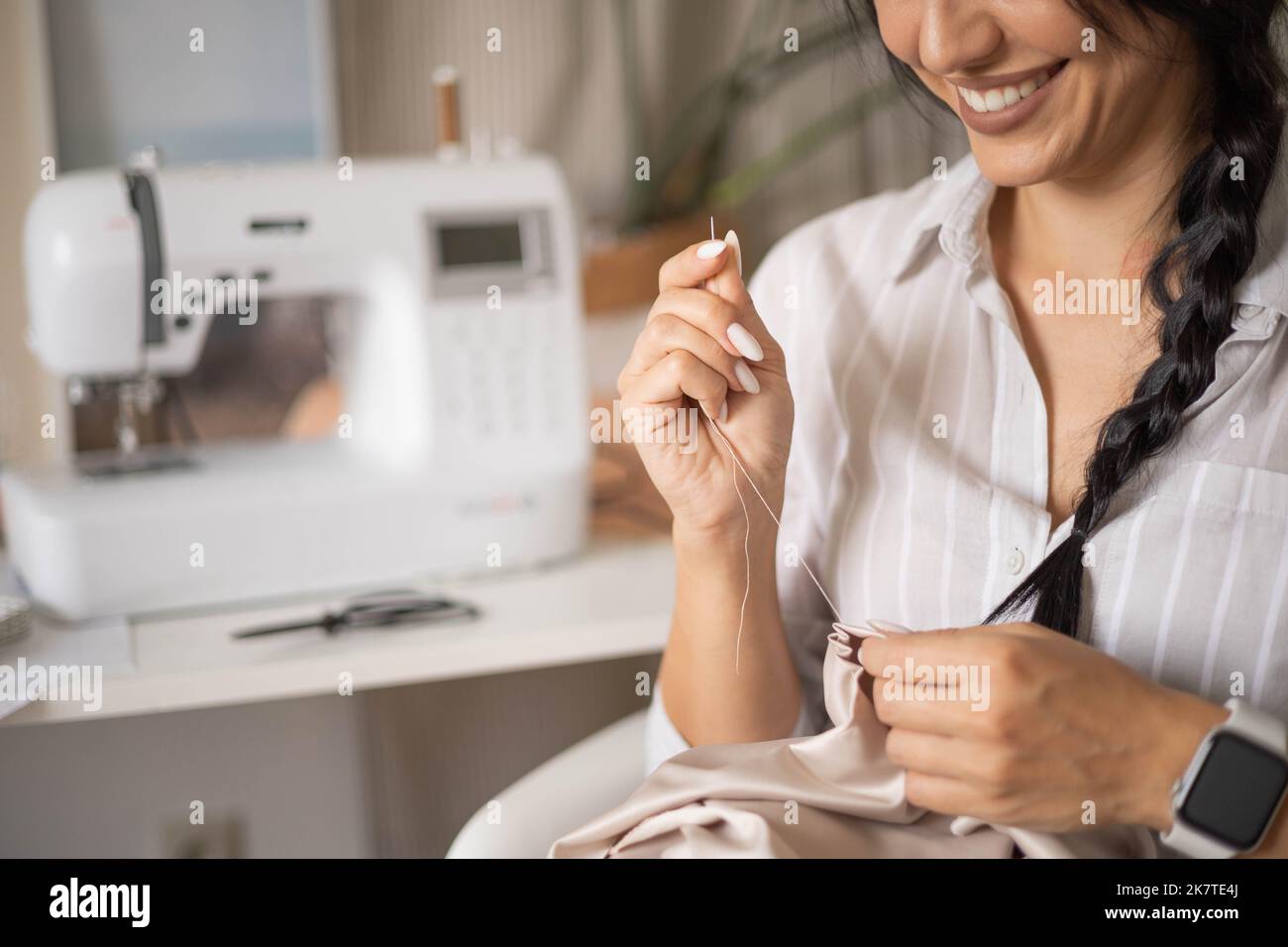 Female tailor hands sewing beige textile with needle and thread process ...