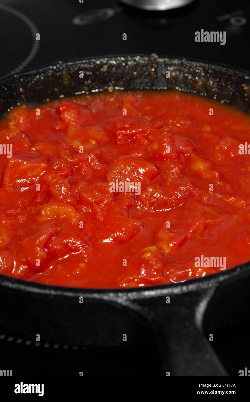 Cooking chopped tomatoes in a cast iron frying pan, on an electric hob ...