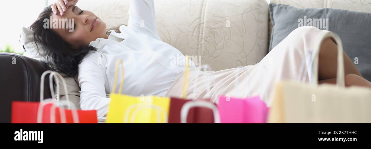 Tired woman after shopping laying on couch at home, bags full with ...