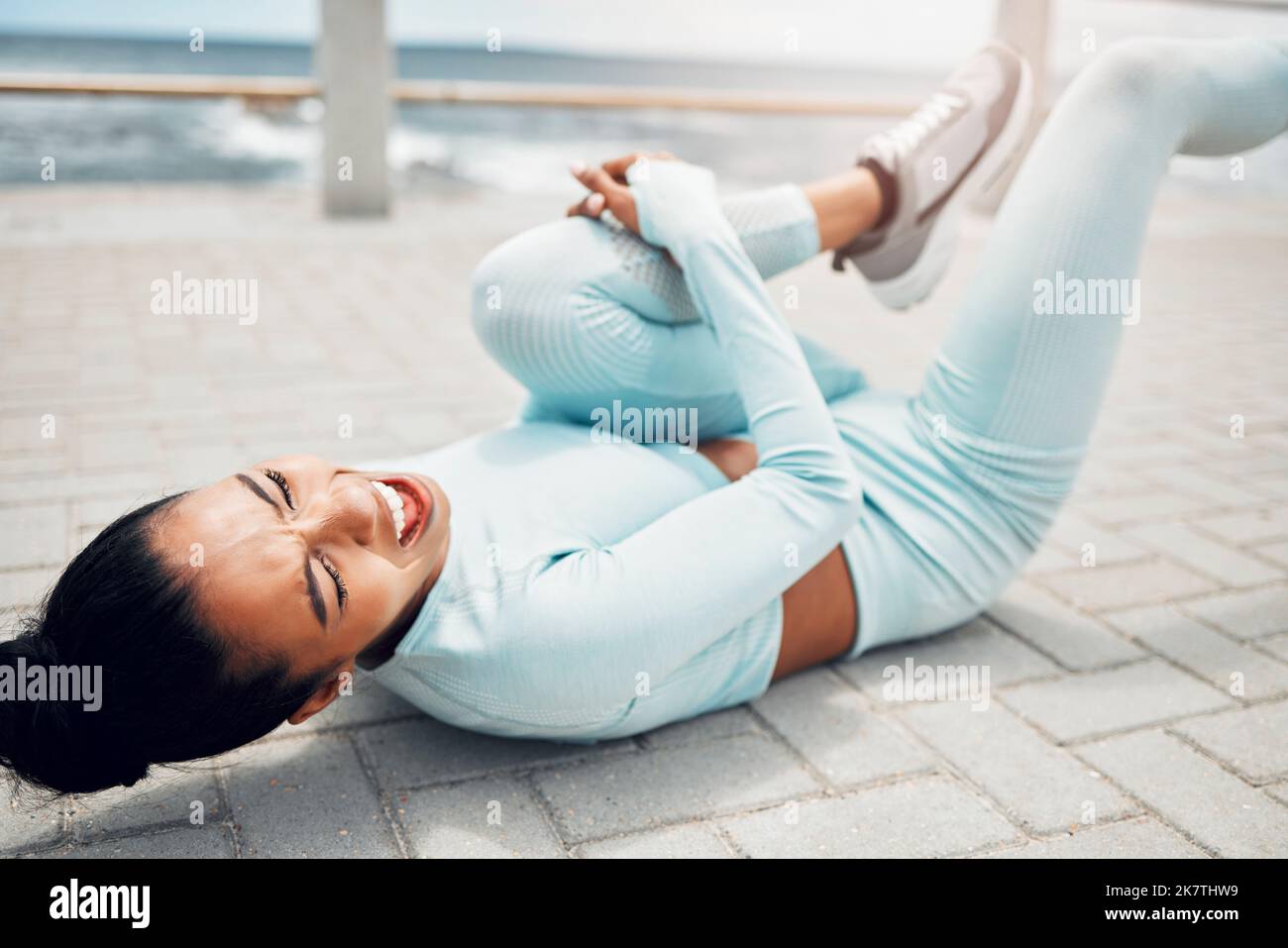 Screaming, leg injury and sports woman lying on path by beach, ocean or ...