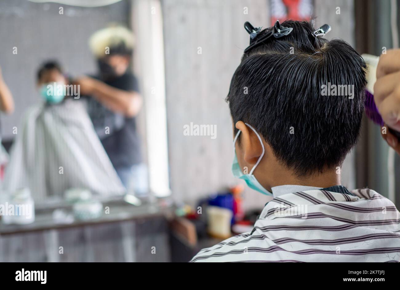 Teenage boy in a face protective mask is getting a haircut from a ...