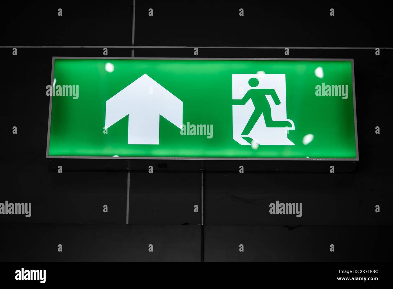 Big Emergency fire exit sign is placed on the black wall over the door ...