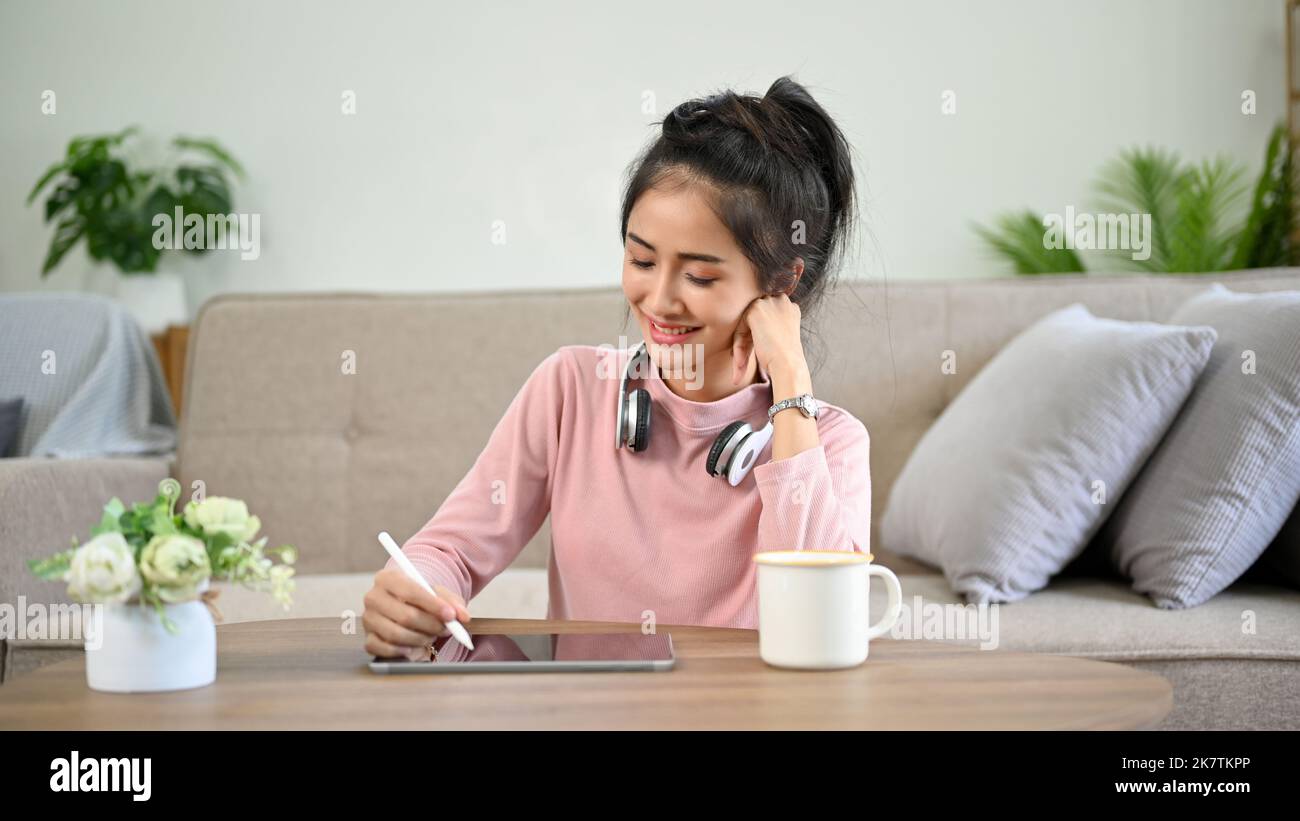 Pretty young Asian girl using her digital tablet touchpad, sitting at ...
