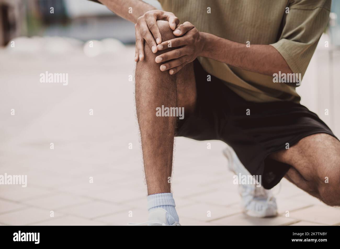 Young man sitting and touching his aching knee Stock Photo - Alamy