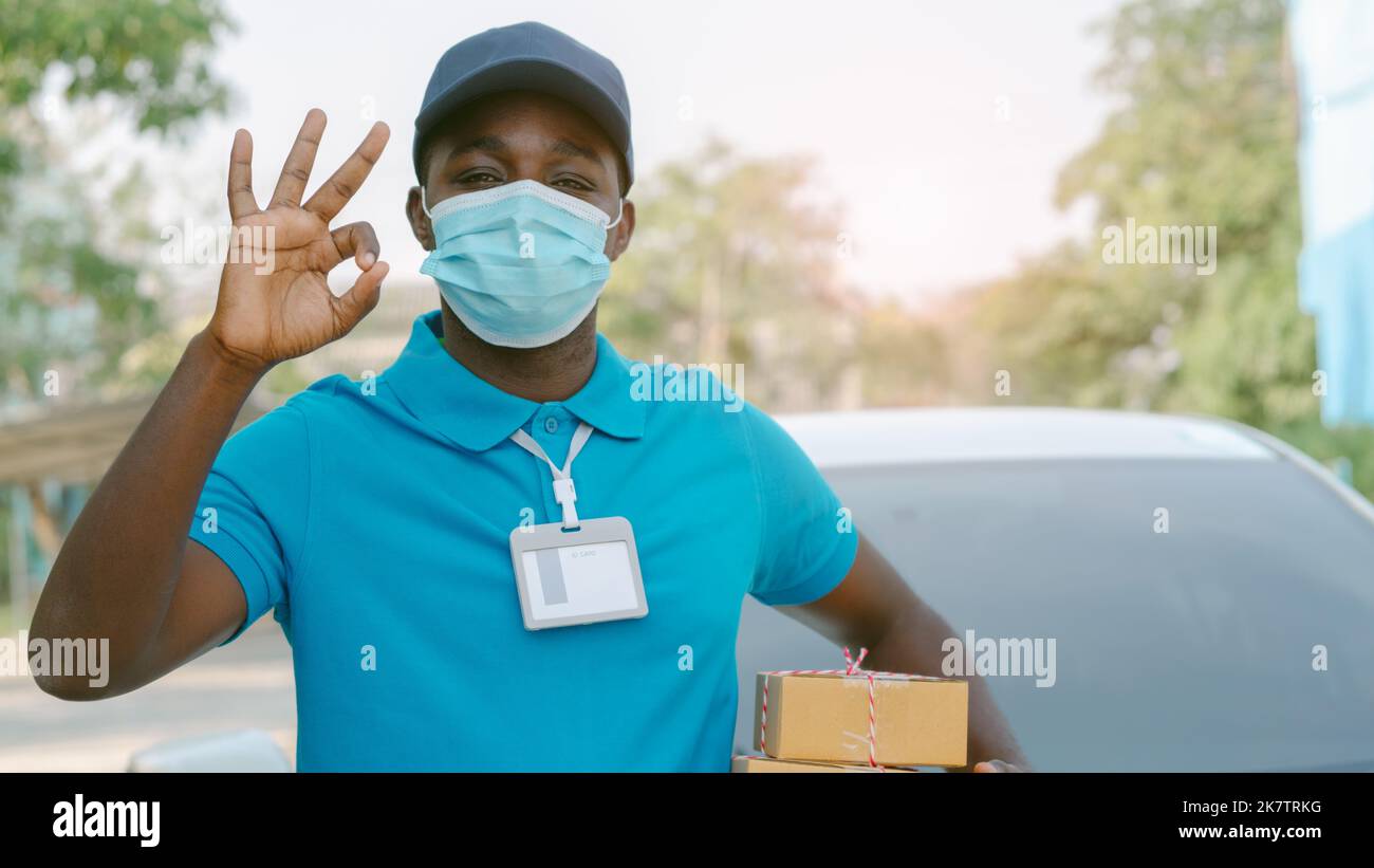Delivery african postman in blue uniform holding package with wearing ...