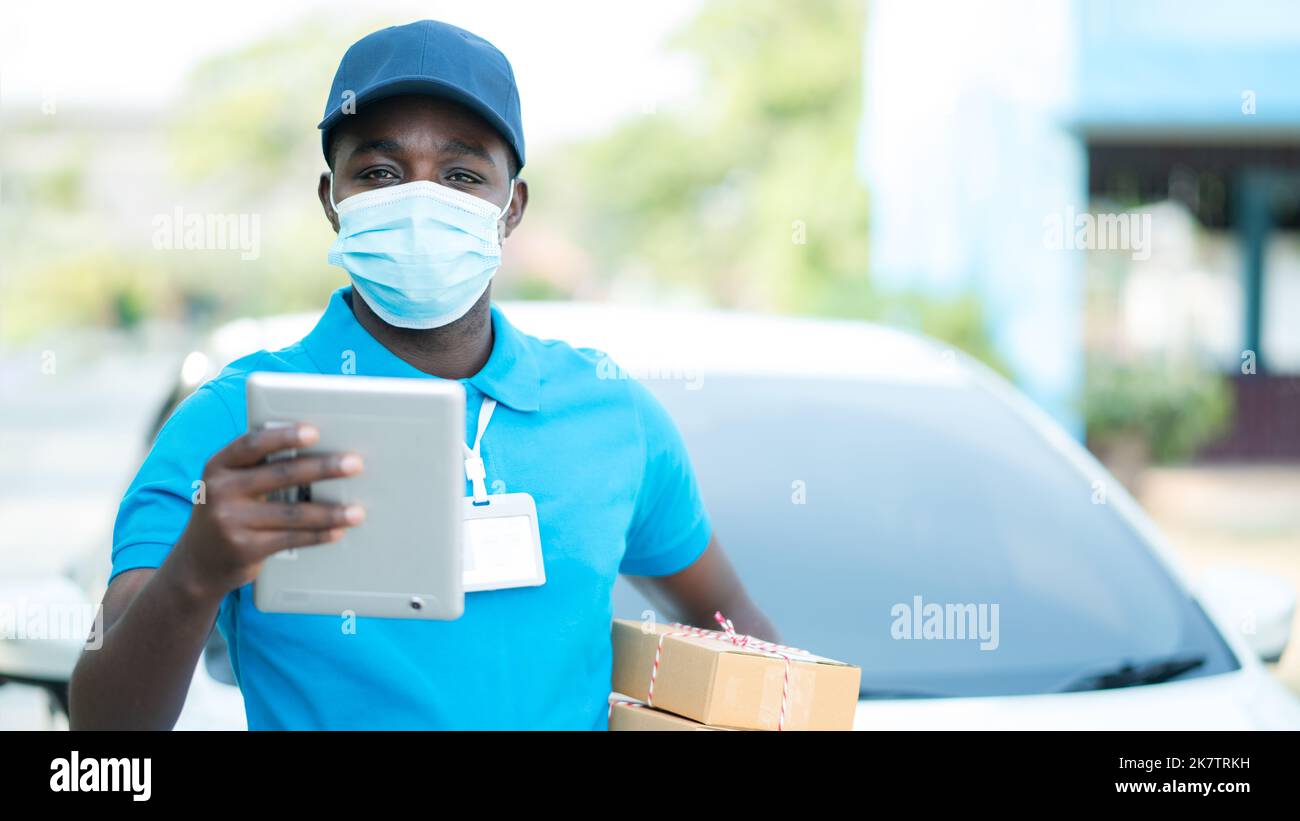 Delivery african postman in blue uniform holding package with wearing ...