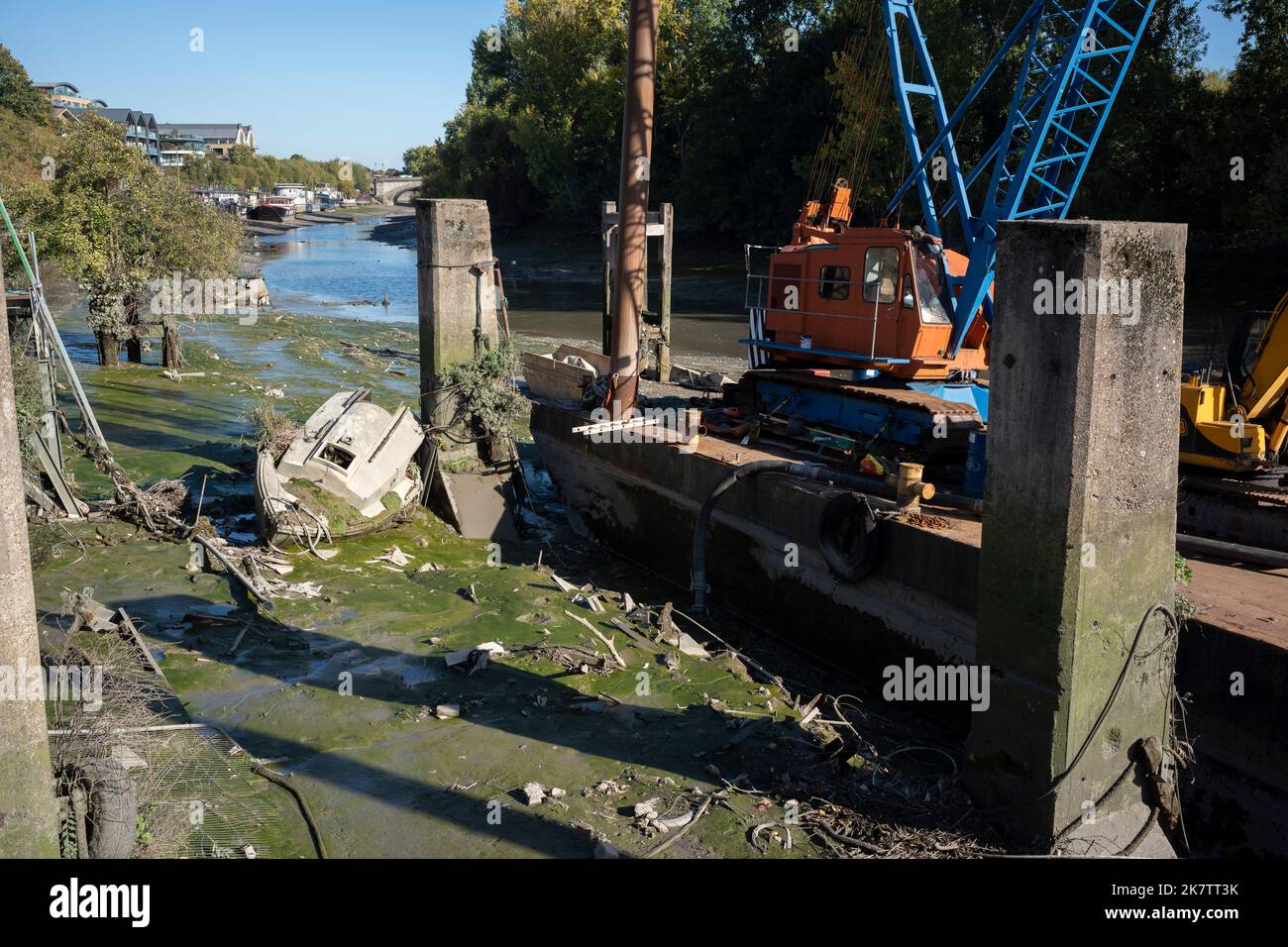 A sunken, derelict boat sits in low-tide river mud and silt at ...