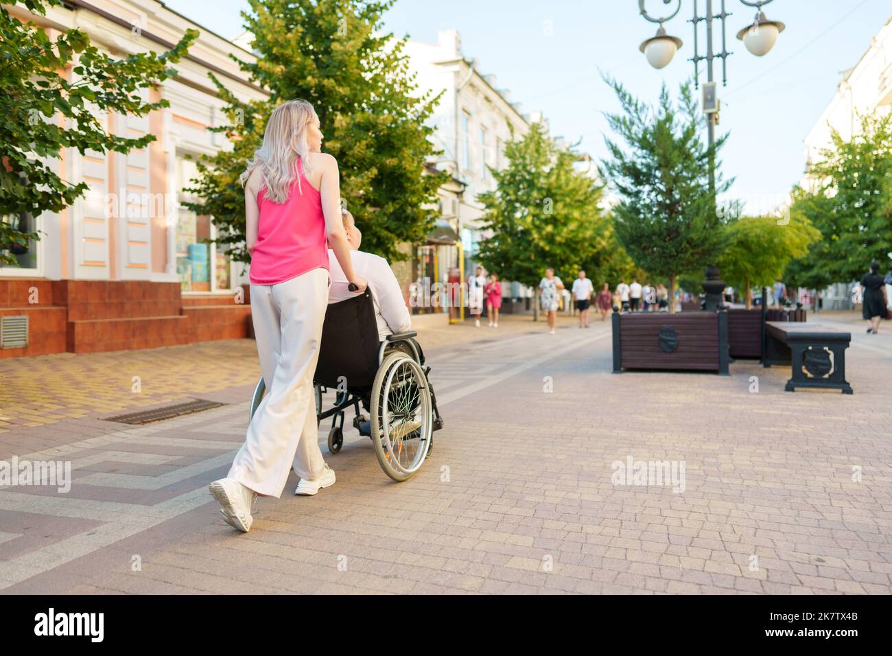 Young female caregiver pushing wheelchair with female person with ...