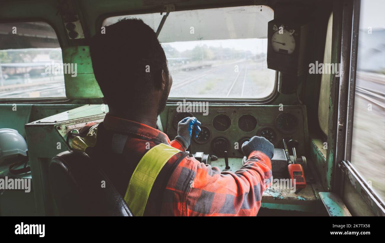 An African train driver is driving the train past a public residence ...