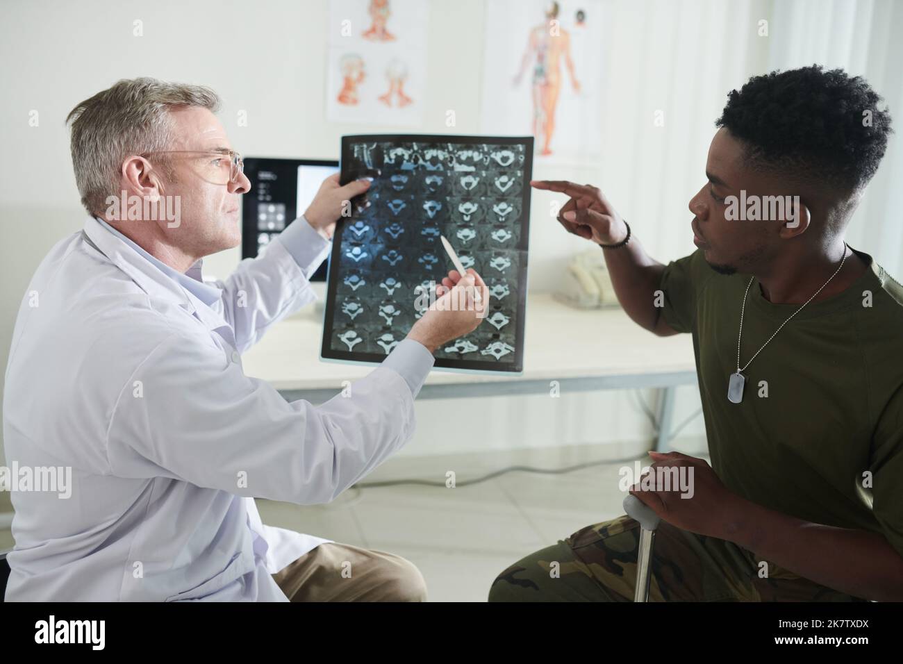 Serious doctor showing MRI image of spine when talking to military man ...