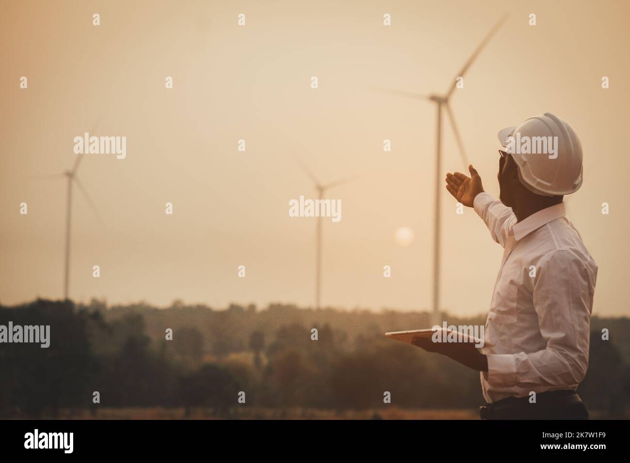 African engineer man stands holding tablet front the wind turbines ...