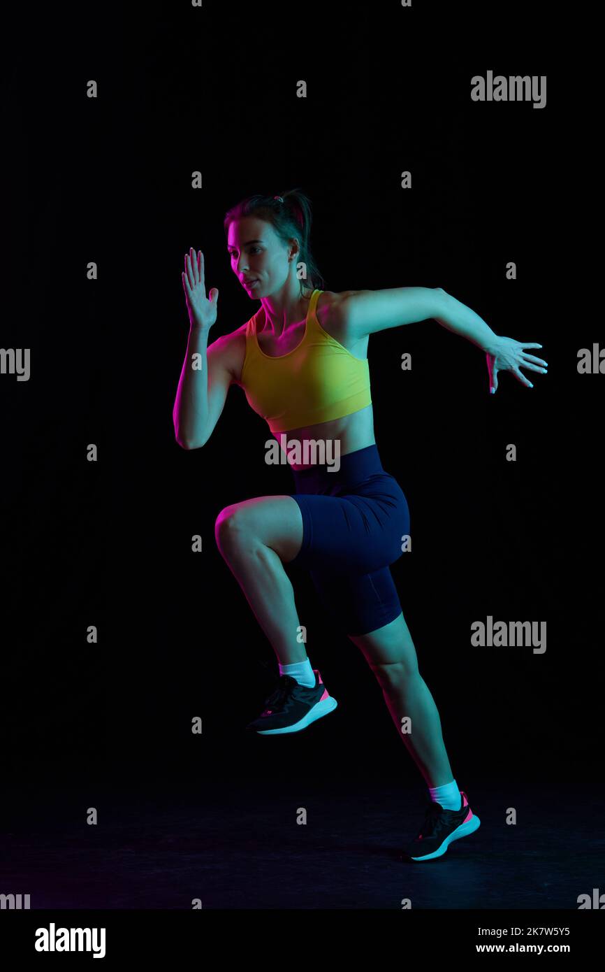 Running technique. Professional female jogger running isolated on dark ...