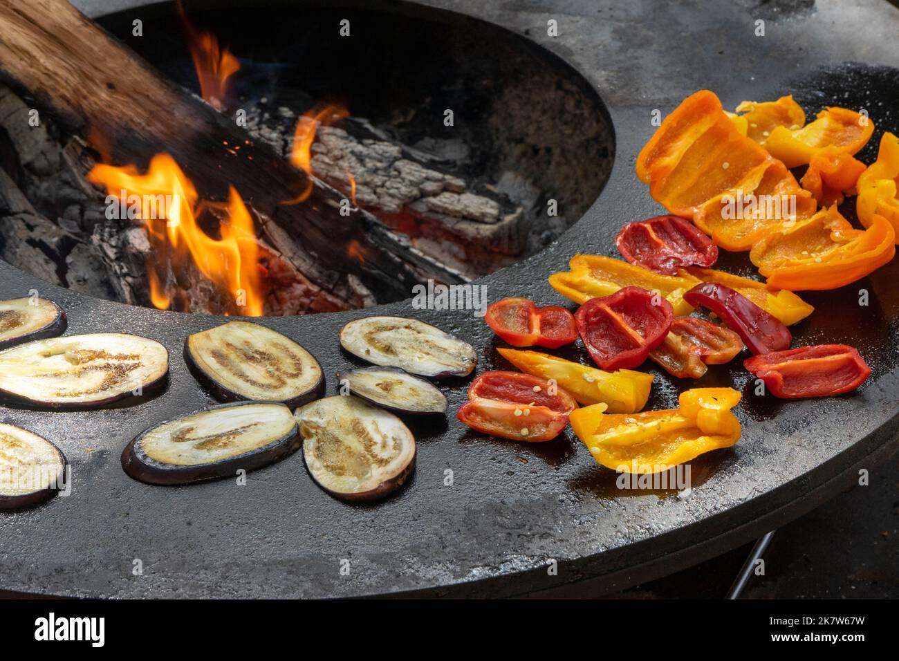 Courgette and red and yellow peppers being cooked over a fire, at a ...
