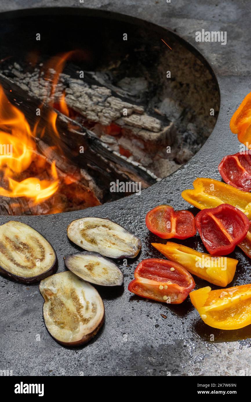 Courgette and red and yellow peppers being cooked over a fire, at a ...